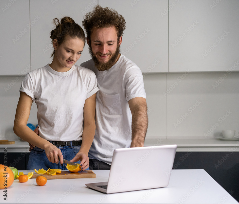 Young couple using laptop at kitchen while cooking and having video ...