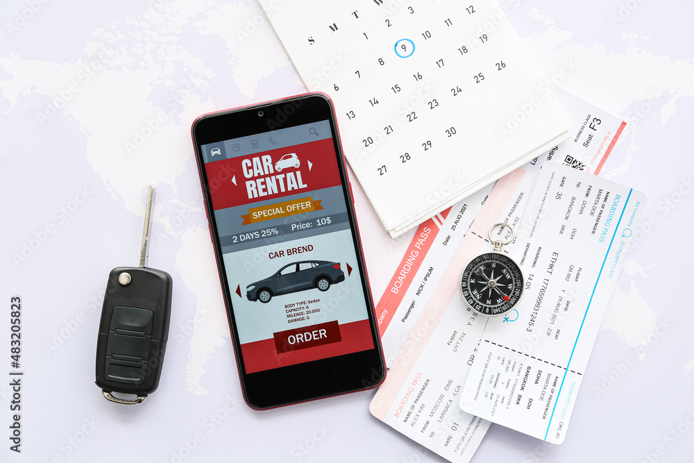 Mobile phone with open car rent app, key, compass and tickets on world ...