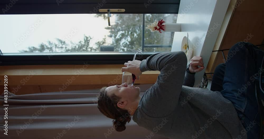 a man with long hair tied up sits in the kitchen near a large window ...