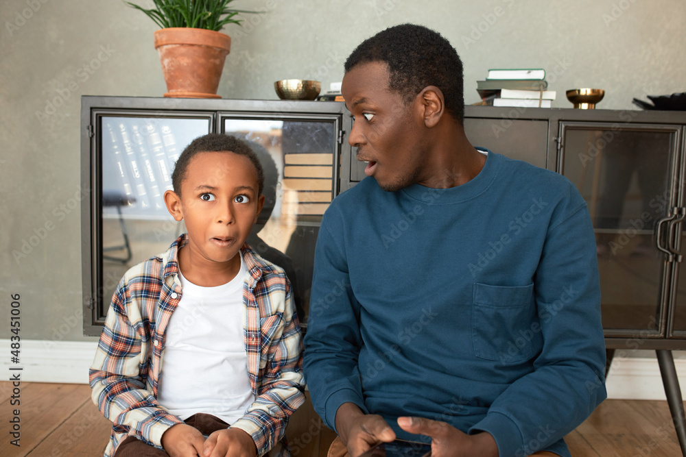 Cute charismatic mixed-race kid in shirt sitting next to his dad with ...