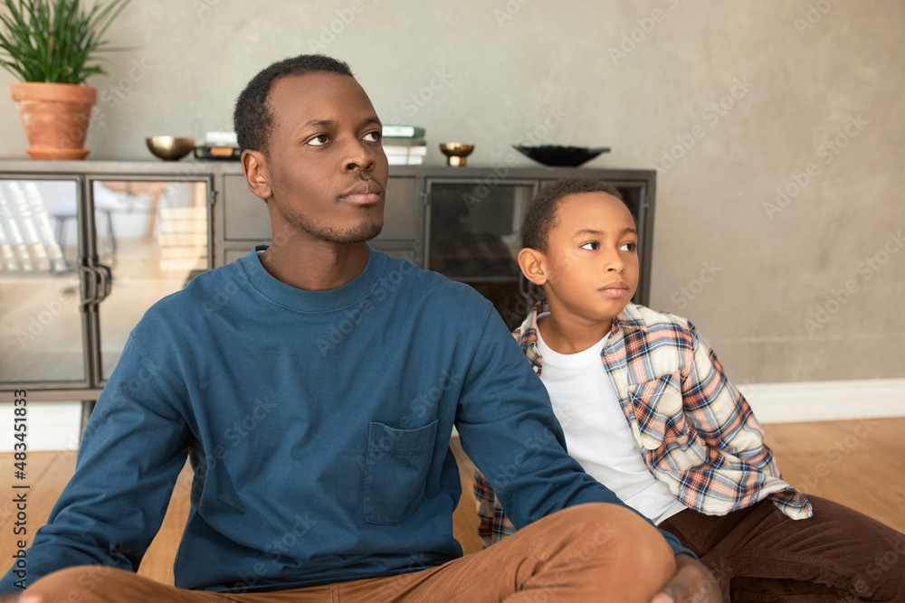 Father and his dark-skinned kid watching TV sitting on floor, having ...
