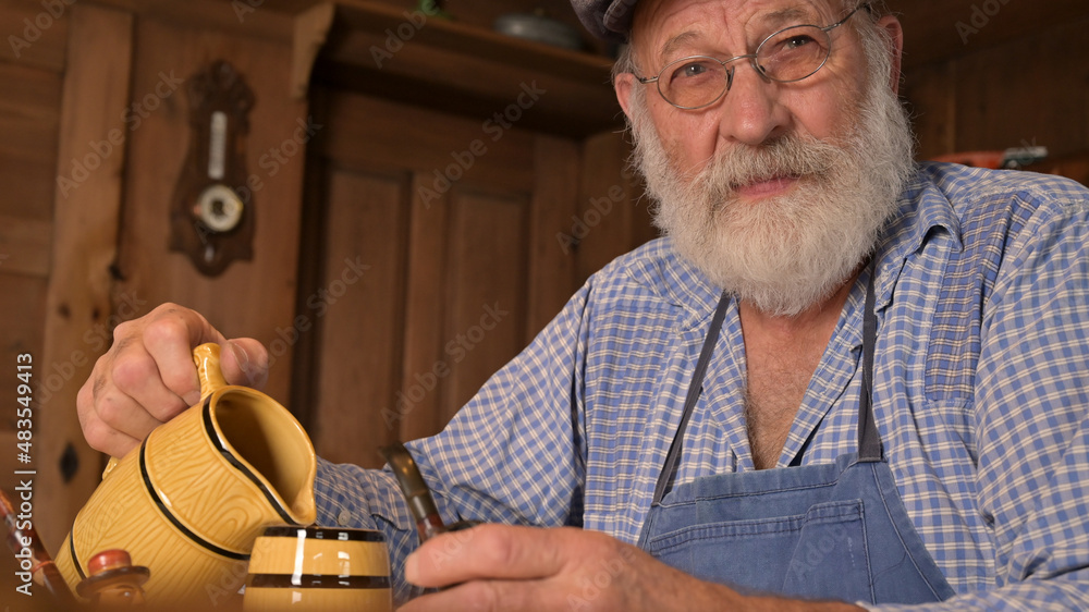 Old man winegrower drinks wine alcohol or cider from a jug and smokes ...