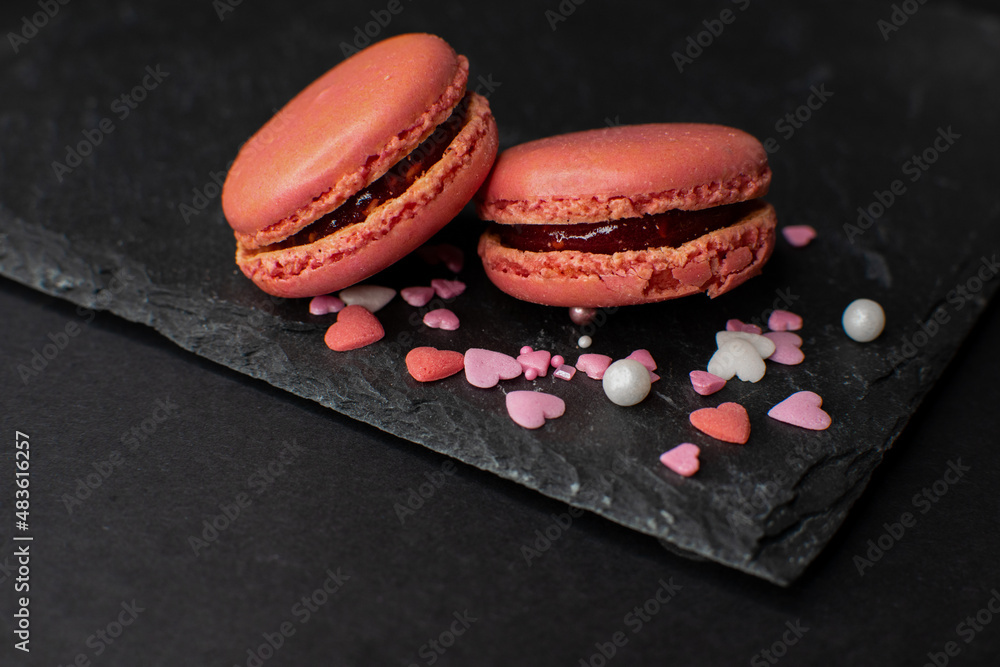 Zwei Pinke Macarons vor dunklem Hintergrund mit Zuckerstreuseln in ...