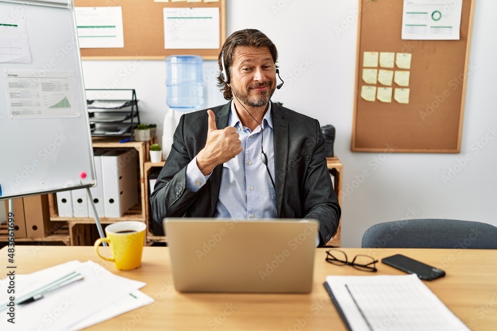 Handsome middle age man wearing call center agent headset at the office ...