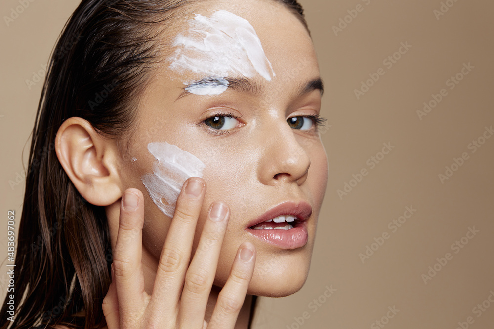 young woman applying a soothing face mask cosmetic beige background ...