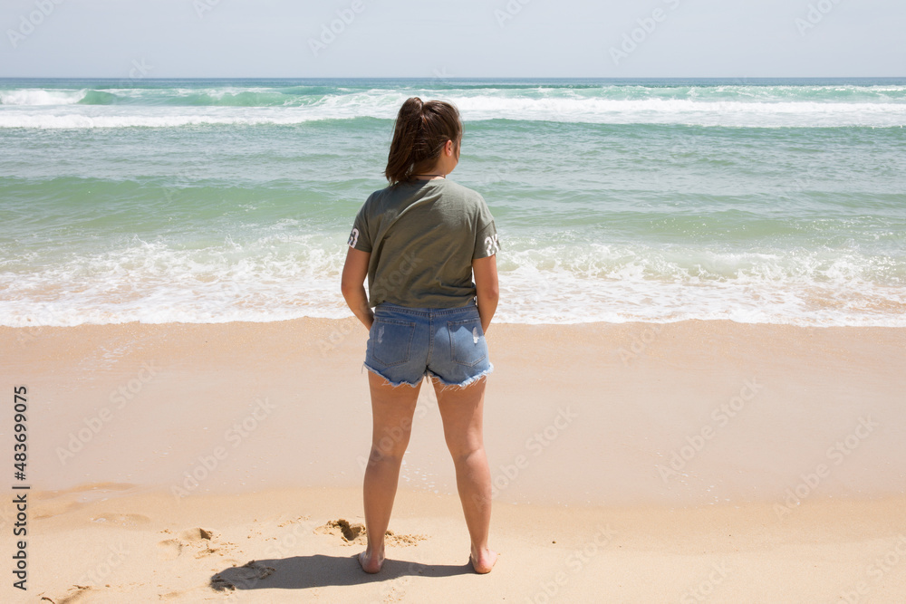 Girl back in short jeans standing at ocean sand beach dreaming on beach ...