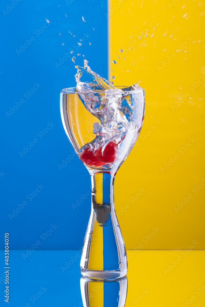 A vertical studio shot of a red cherry being dropped from a height into ...