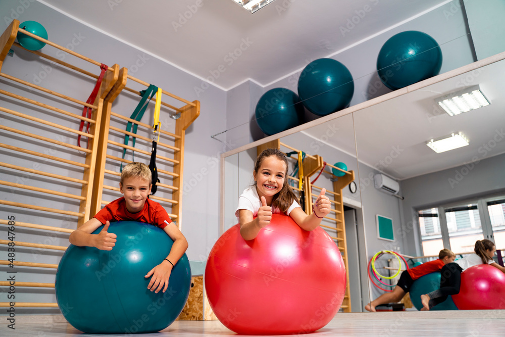 Toddlers boy and girl laying on swiss balls in the gym and showing ...