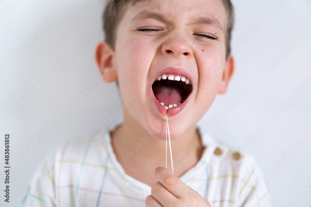 Cute boy pulling loose tooth using a dental floss. The boy's first milk ...