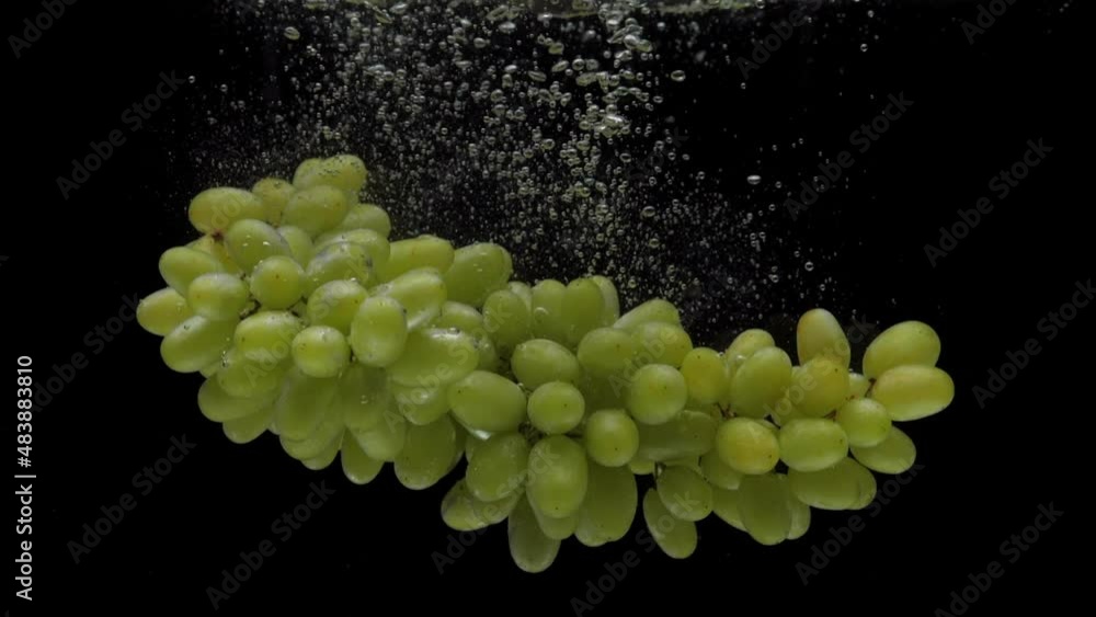 Slow motion green grapes falling into transparent water on black ...