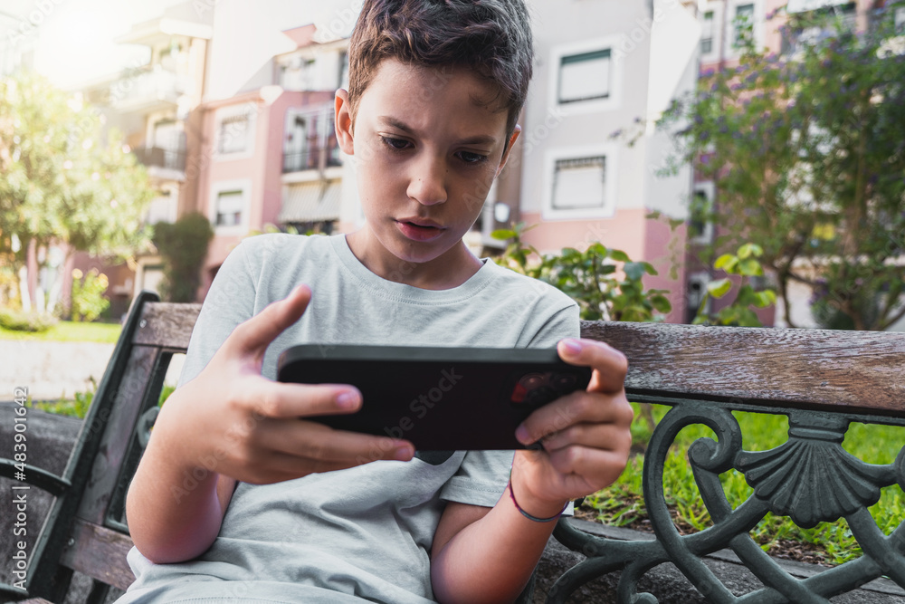 addicted little boy using smartphone application sitting on a bench in ...