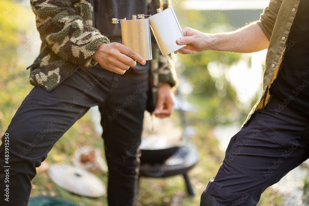 Two men cheering with flasks while fishing on lake, close-up on flask ...