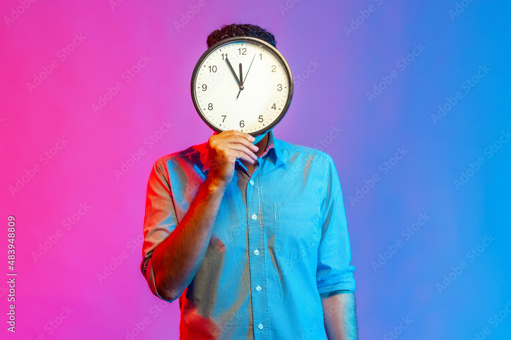 Portrait of man in shirt hiding face behind big wall clock display ...