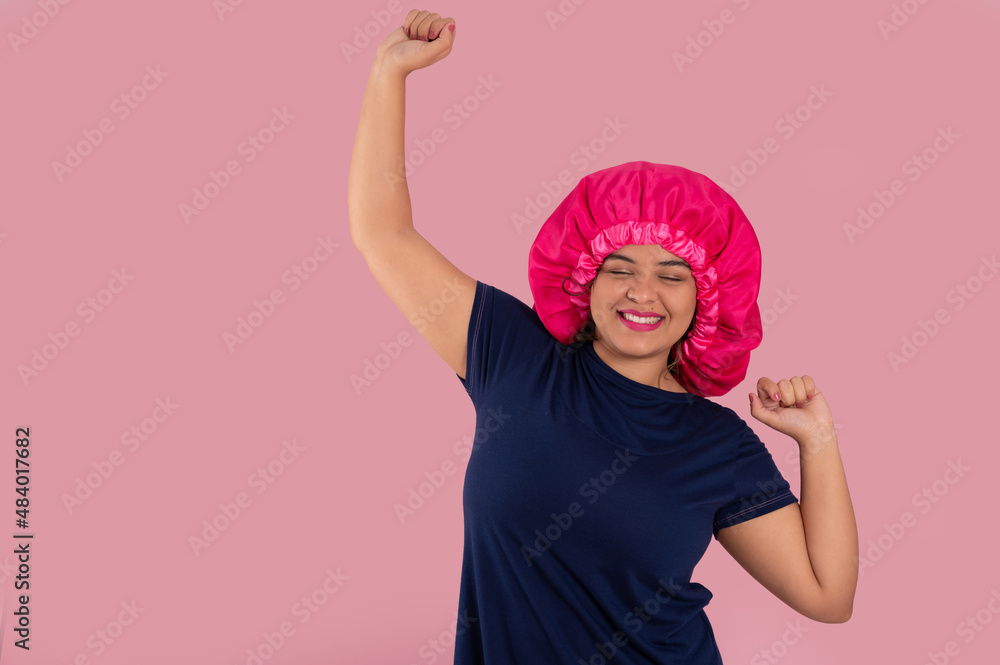 Sleepy woman stretching, wearing a pink shower cap, smiling, with the ...