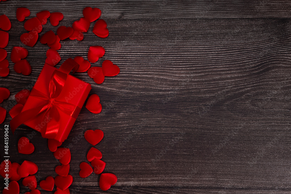 A red box with a gift in small red hearts on a wood background, a ...