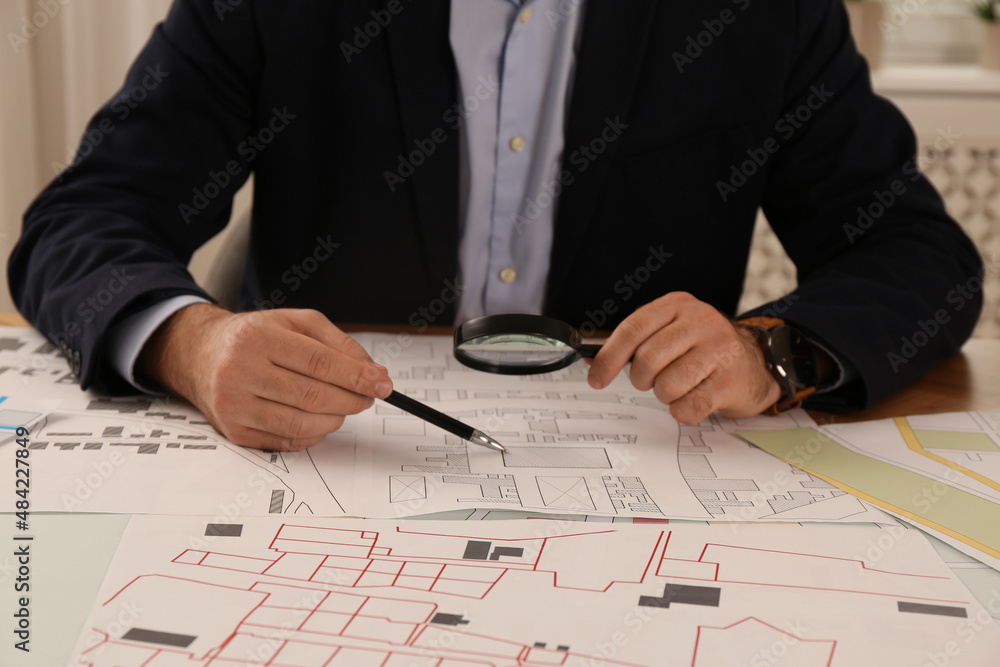 Professional cartographer working with cadastral map at table in office ...