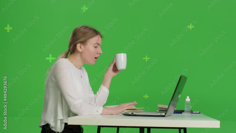 Young woman works with a computer at her desk over green screen ...