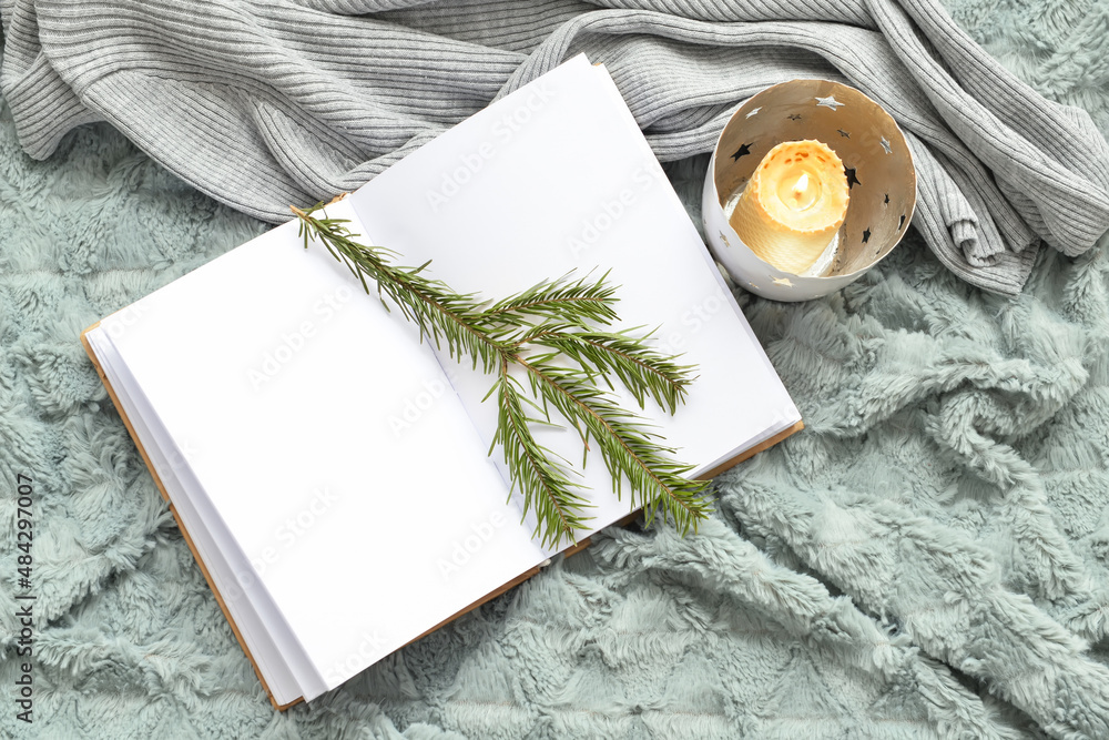 Burning candle, book with blank pages and fir tree branch on soft plaid ...
