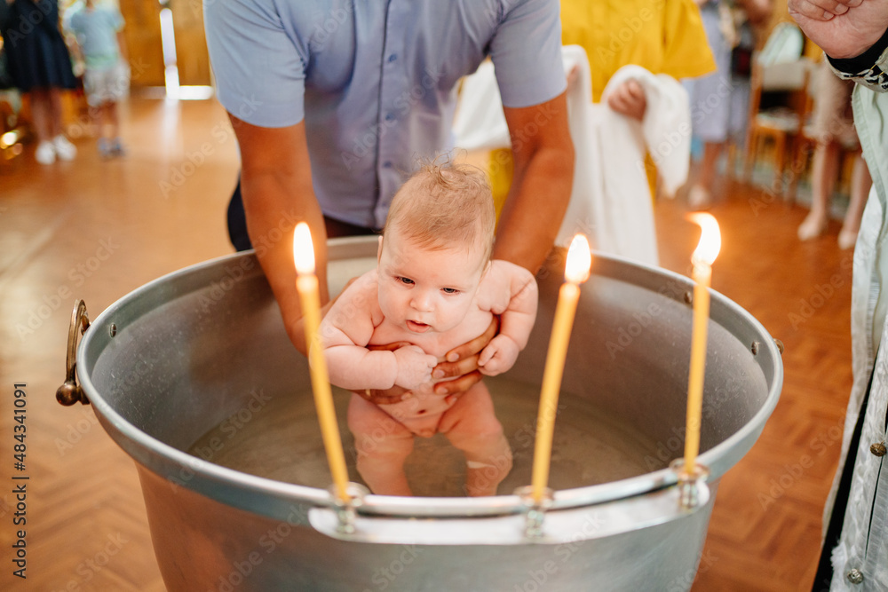 the baby boy is lowered into a font with holy water at baptism in the ...