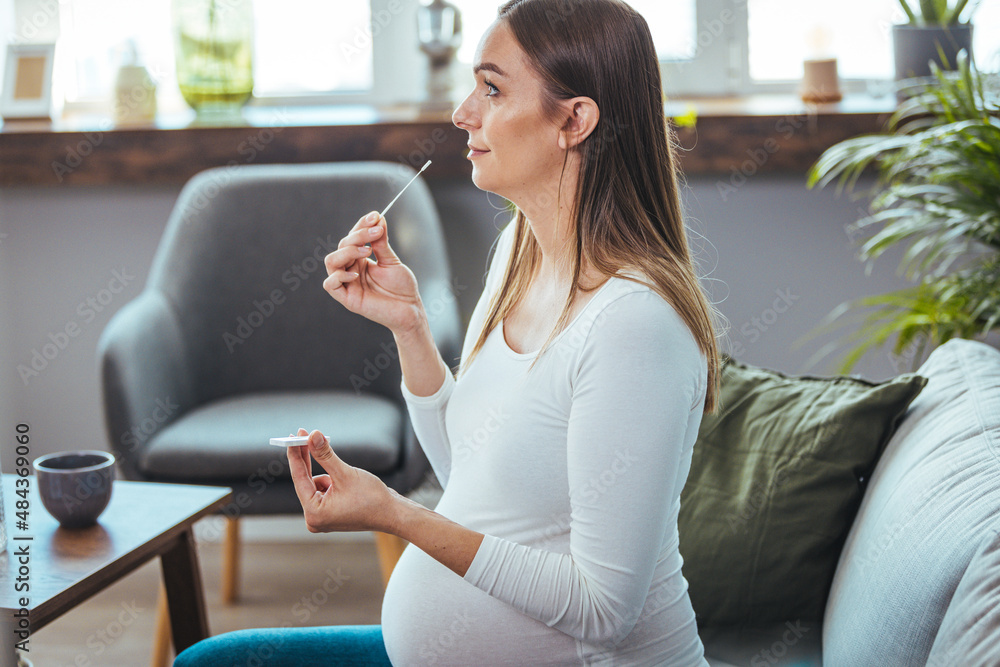 Portrait pregnant woman sitting, doing a auto test for COVID-19 at home ...