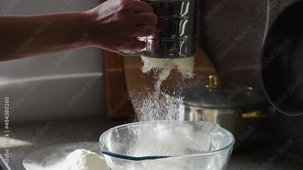 Close up footage of hand sifting white flour into glass bowl with a ...