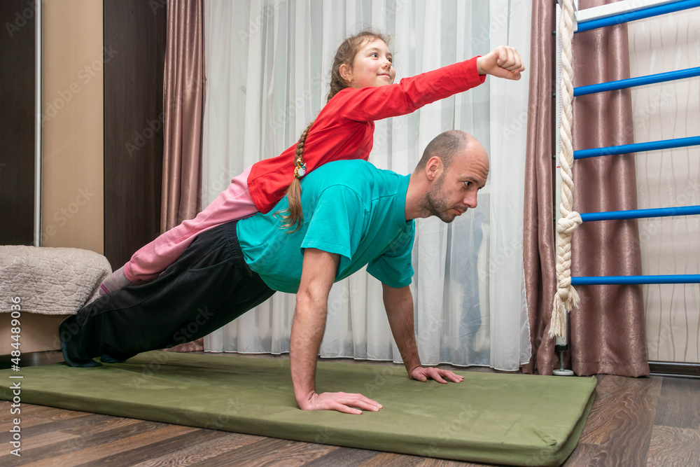 Foto de Dad does push-ups at home with his daughter on his back. A man ...