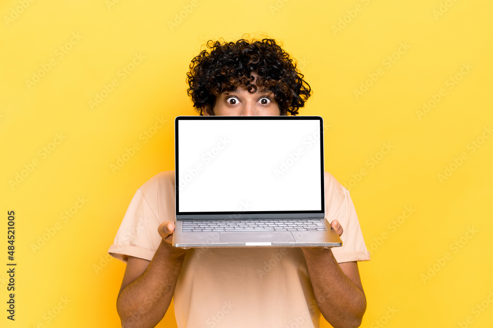 Shocked indian guy, peeking out from behind laptop, looks surprised at ...