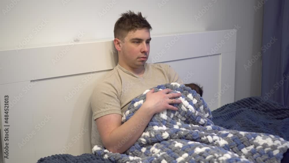 An exhausted young dad cradles a child in his arms in bed. A man with a ...