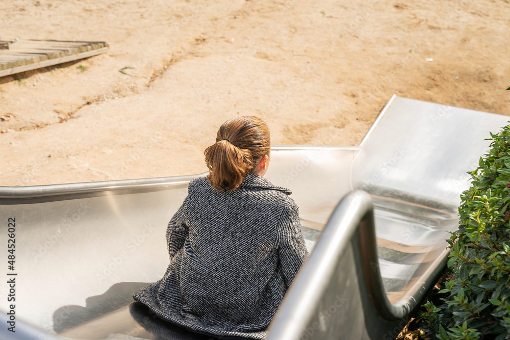 Caucasian girl with her back to camera sliding down a metal slide in an ...
