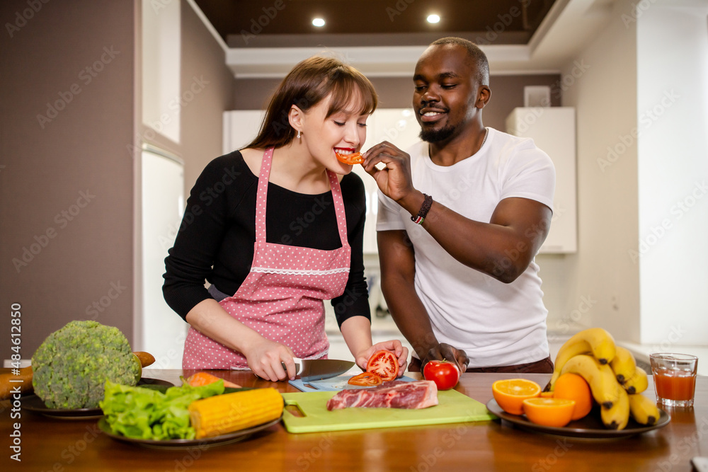 European girl with a dark-skinned man preparing food in the kitchen ...