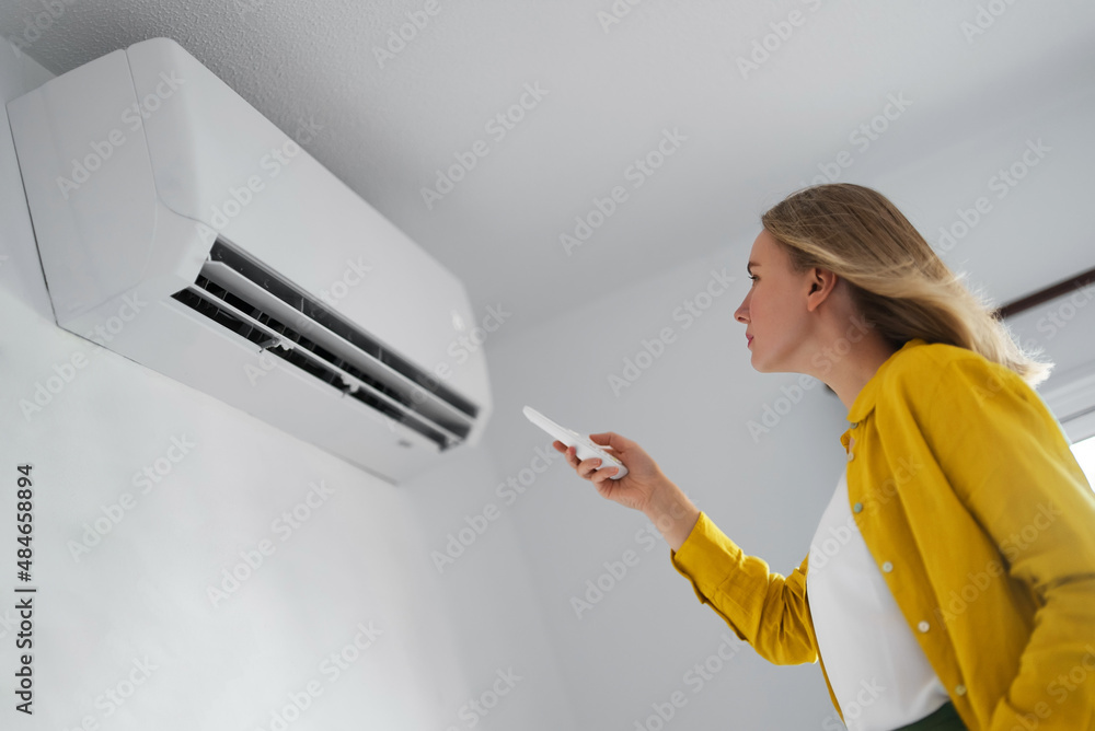 Woman holding remote control aimed at the air conditioner. Stock Photo ...
