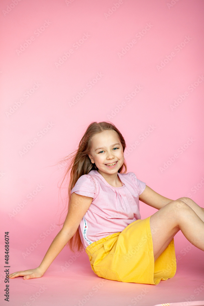 A funny little blonde girl of 10 years old in everyday bright clothes ...