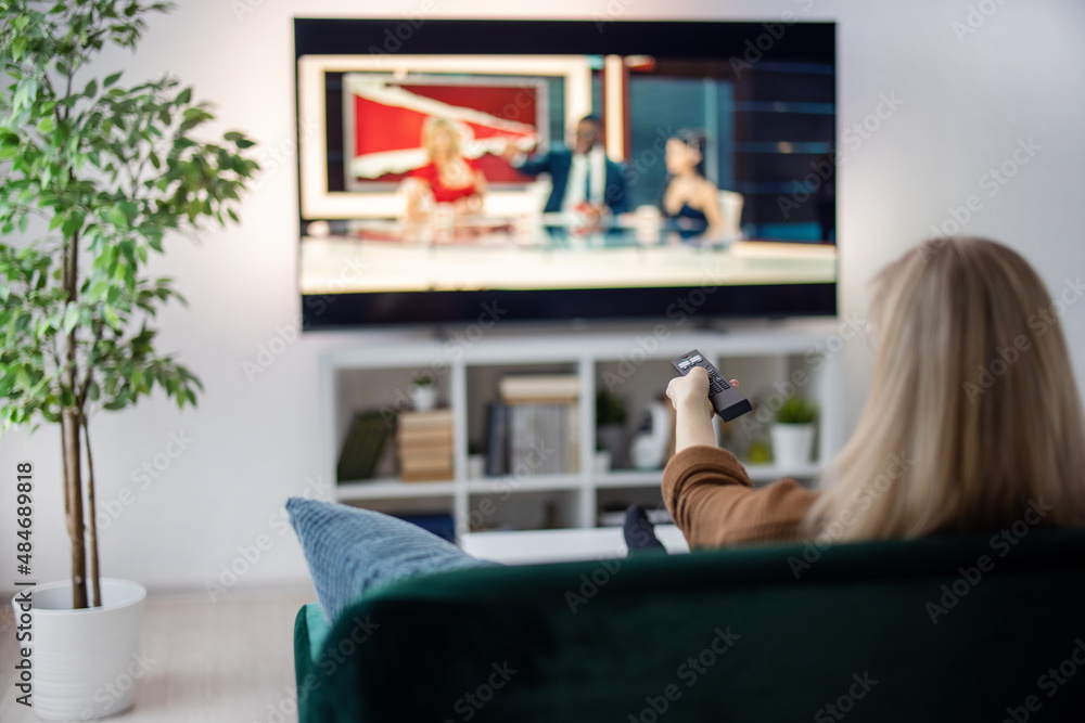 Back view of woman with blond hair sitting on comfy couch and using ...