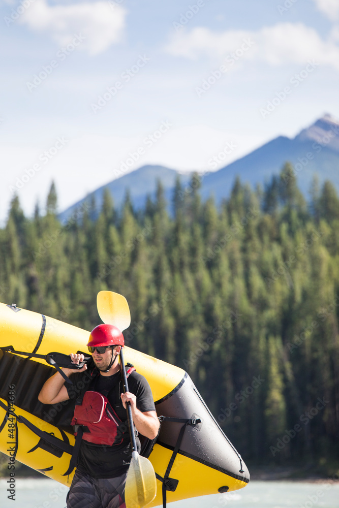 Scenic image of man carrying yellow raft (packraft) in wilderness ...