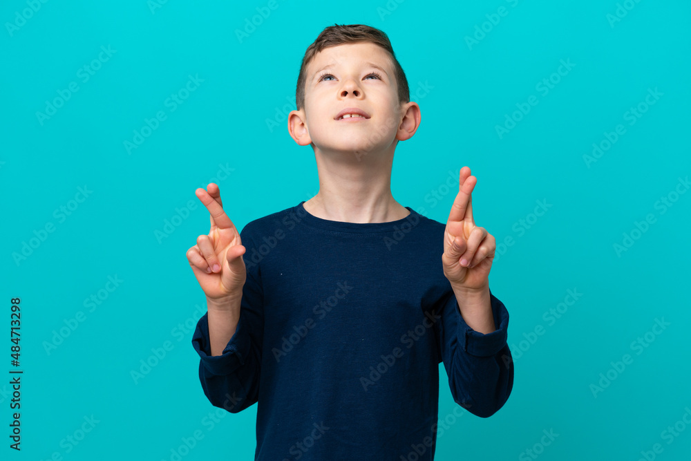 Little kid boy isolated on blue background with fingers crossing and ...