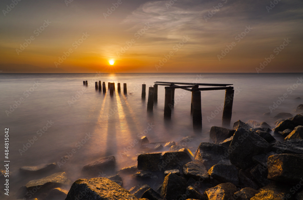 Beautiful sunset scenery at the beach with a view of a jetty pillars ...