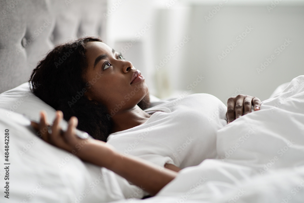 Unhappy black woman laying in bed, staring at the ceiling Stock Photo ...