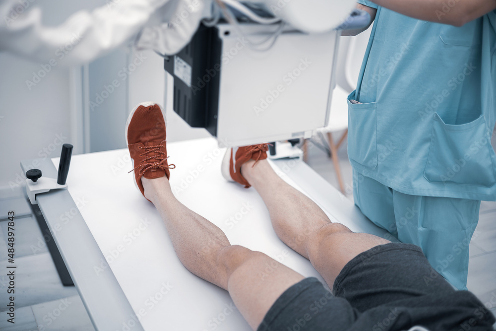 A young man undergoes an x-ray radiograph to identify knee pain in a ...
