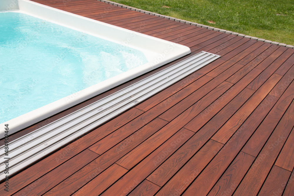Teak wood pool deck, decking installed around the blue swimming pool ...
