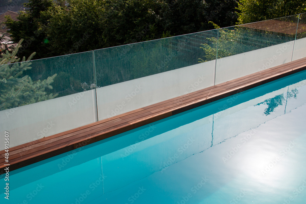 Infinity swimming pool with glassy safe fence and hardwood decking edge ...