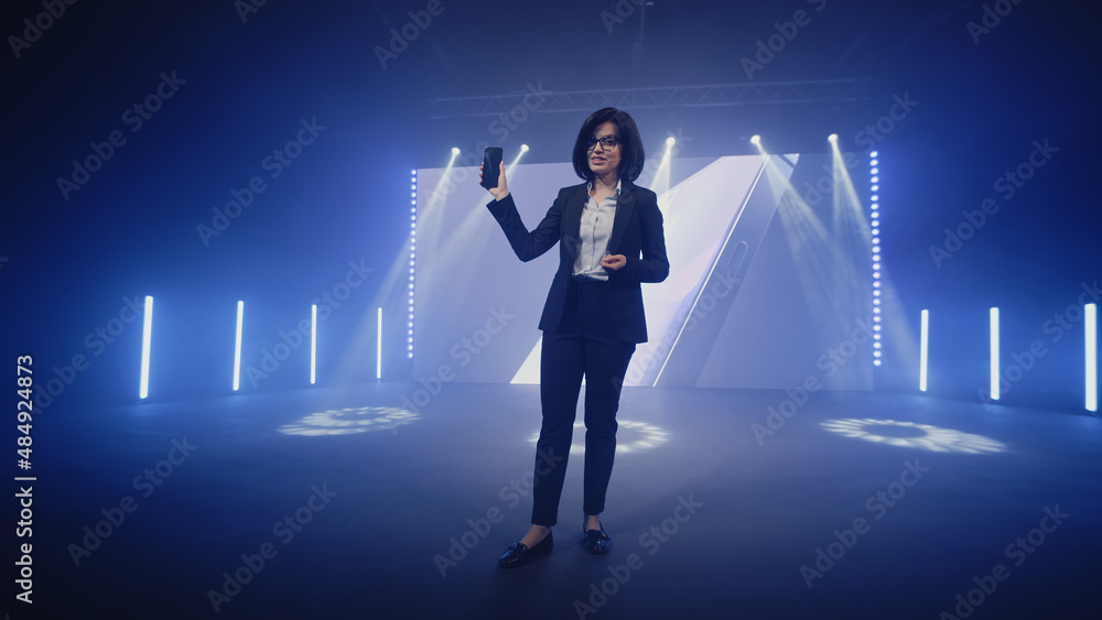 Female host in a suit on stage showing a new fashionable device, during ...