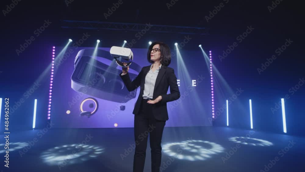 A female presenter standing on stage in modern studio with LED screen ...