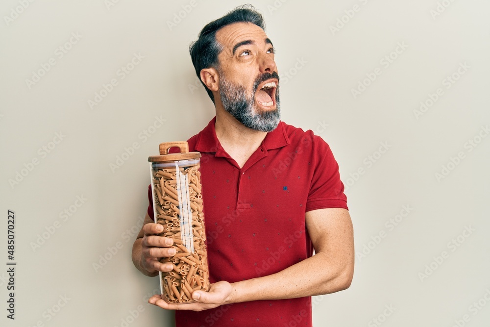 Middle age man with beard and grey hair holding jar with macaroni pasta ...