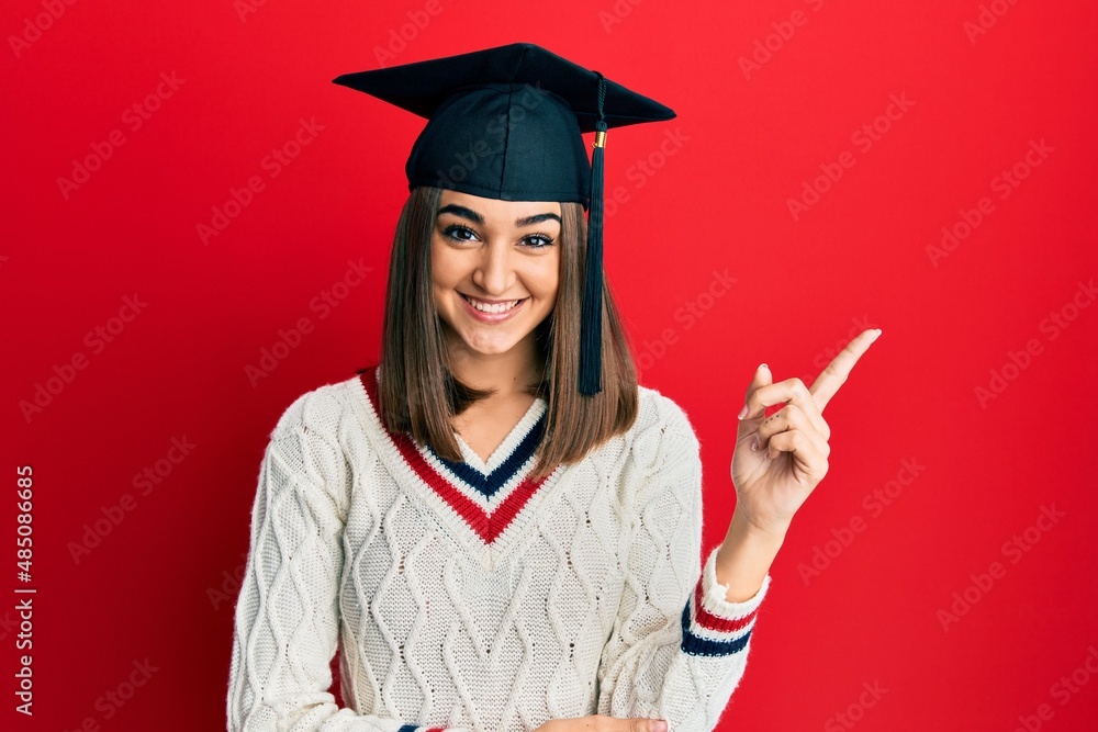 Young brunette girl wearing graduation cap smiling happy pointing with ...