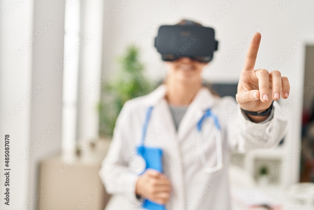 Young blonde woman wearing doctor uniform using touchpad and vr goggles ...