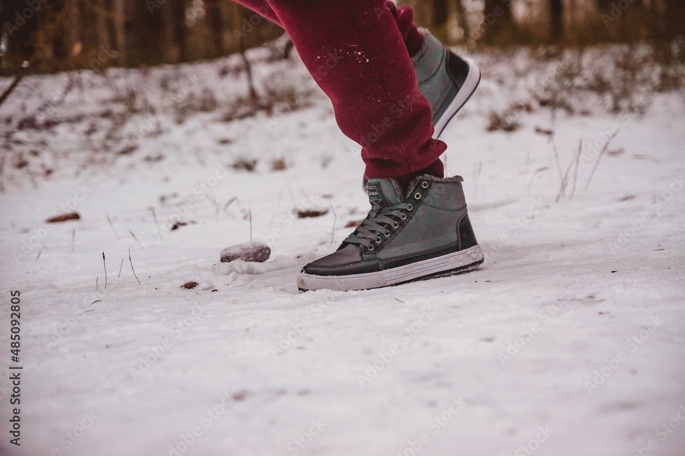 The girl's feet in sneakers are running along the snow path. A sports ...