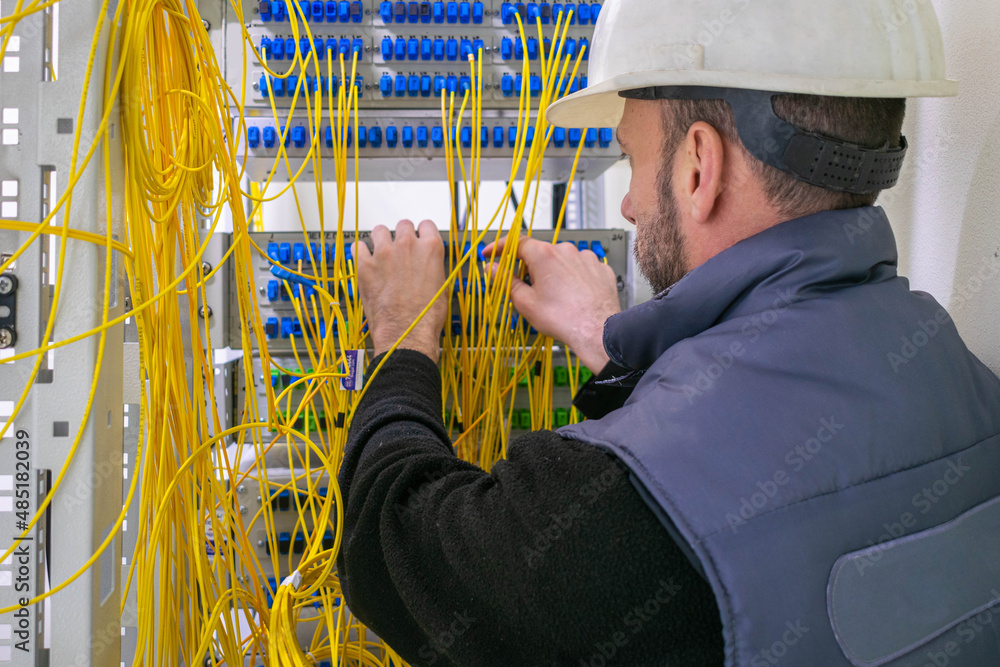 engineer works in data center server room. A man lays fiber optic wires ...