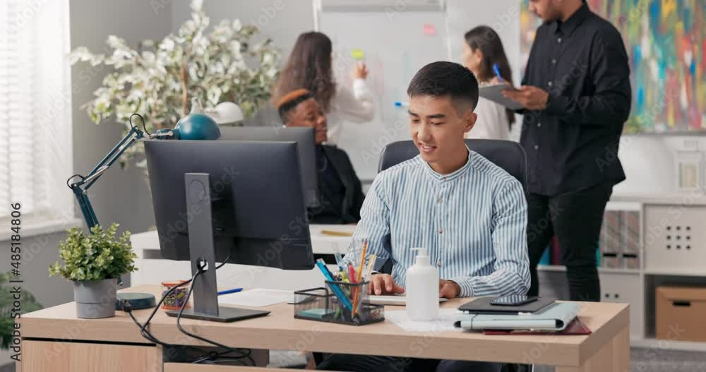 A man of Asian Korean beauty sits in front of an office computer, using ...