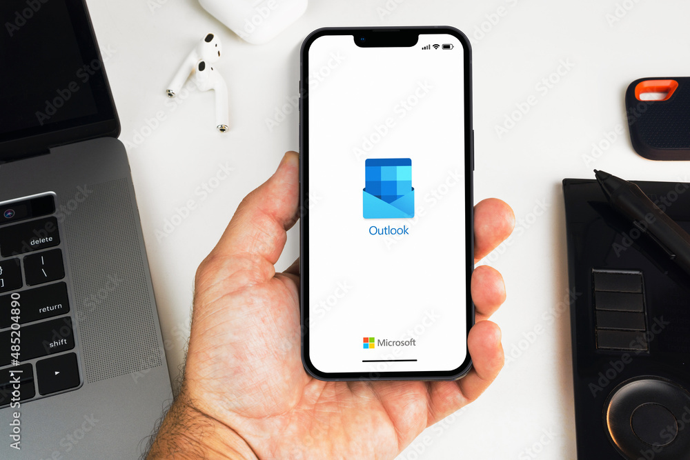 Male hand holding a smartphone with Microsoft Outlook app on the screen ...