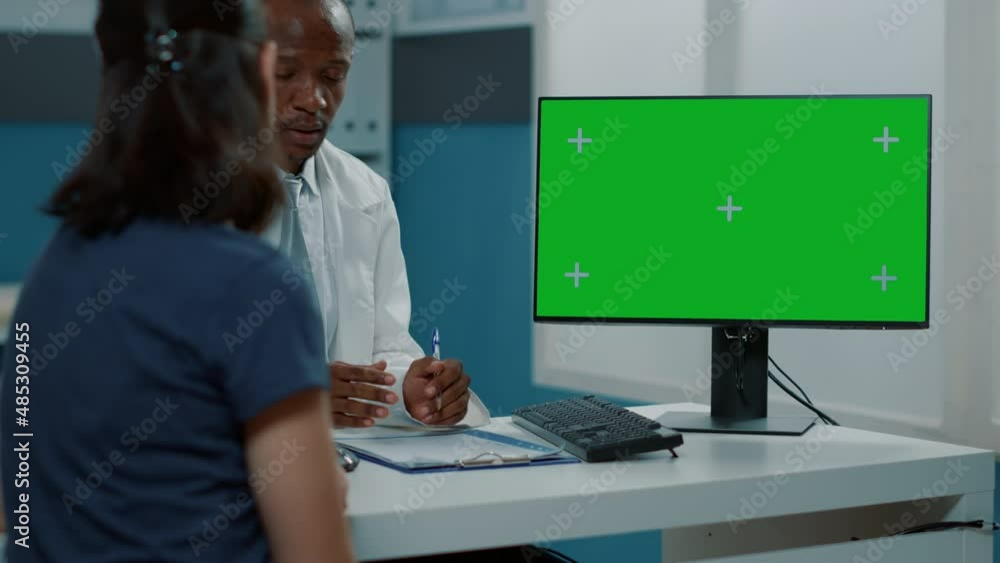 Doctor and adult looking at computer with green screen on desk at ...